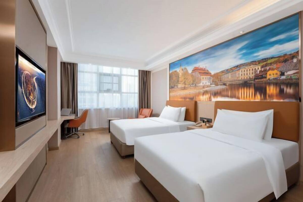 Quarto de hotel com duas camas, uma mesa, uma cadeira e um quadro grande representando uma paisagem fluvial.