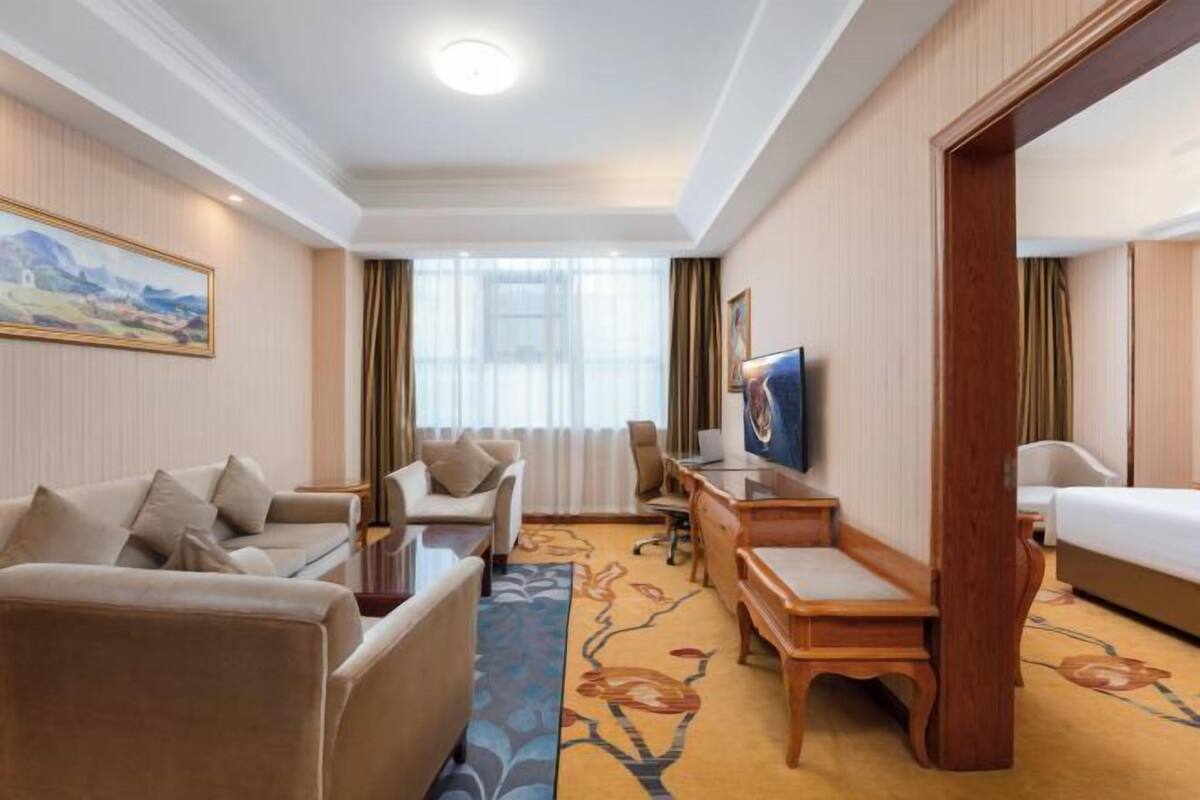 Quarto de hotel com sofá, escrivaninha, televisão e cama.