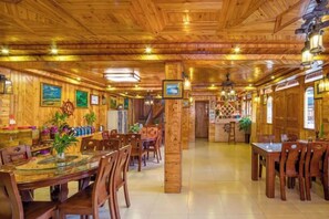 Uma sala de jantar com painéis de madeira, mesas e cadeiras, um bar e uma escadaria para um andar superior.