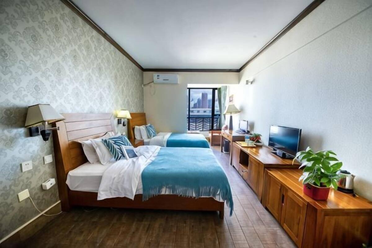 Quarto de hotel com duas camas, televisão, escrivaninha e uma planta em vaso.