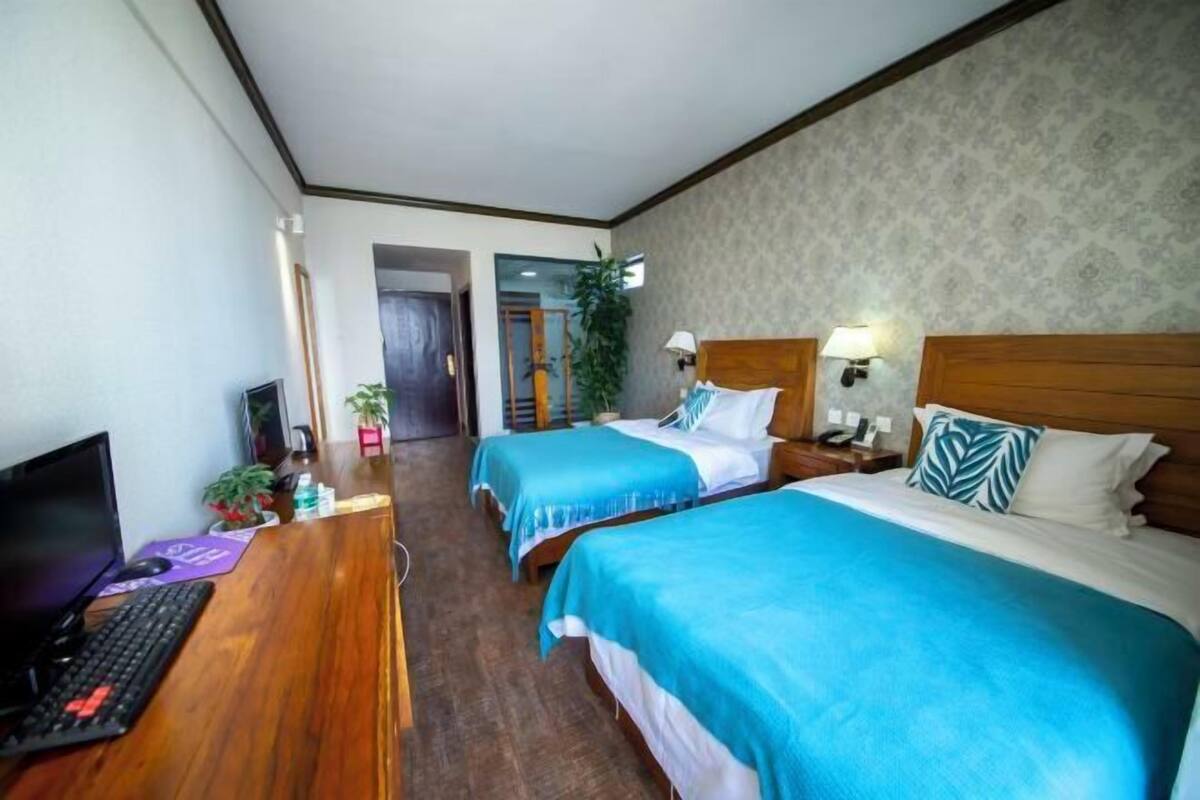 Quarto de hotel com duas camas, uma mesa com computador, televisão e uma planta.