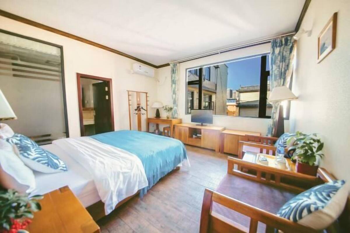 Quarto de hotel com cama, escrivaninha, cadeira, televisão e uma janela grande.