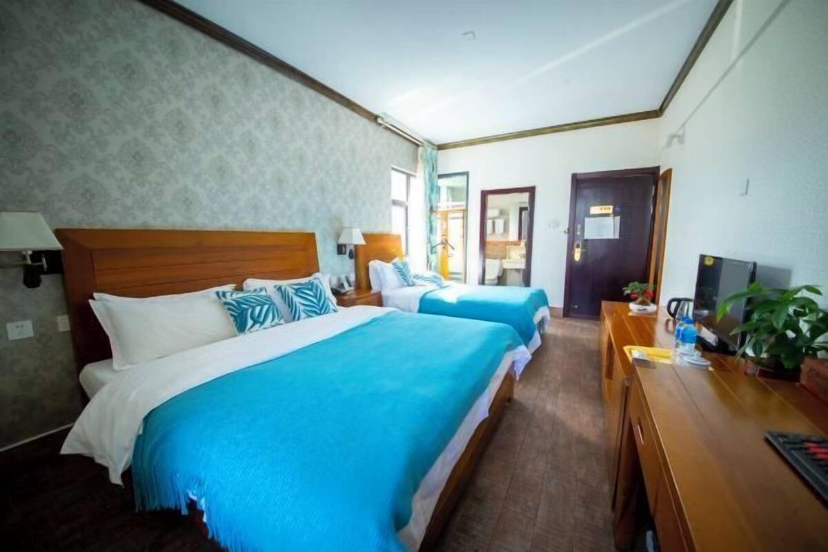 Quarto de hotel com duas camas, cabeceira de madeira, escrivaninha com cadeira e um espelho.