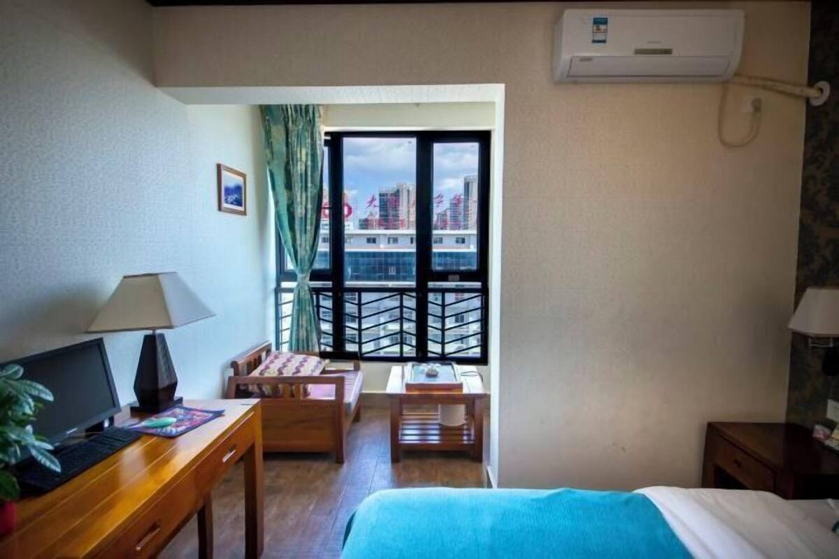 Quarto de hotel com cama, escrivaninha com computador, cadeira, mesinha e janela com vista para edifícios.