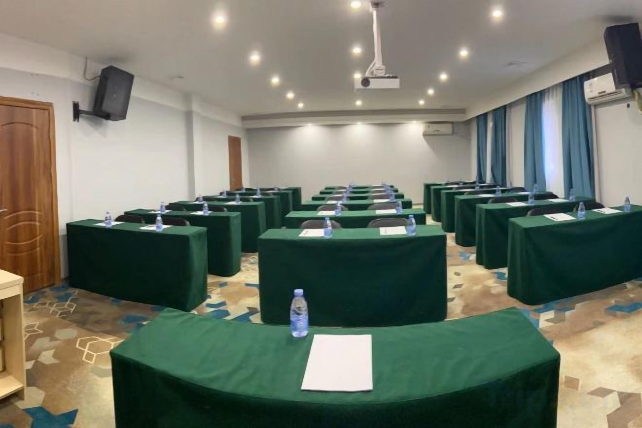 Sala de conferências com fileiras de mesas, cada uma com uma garrafa de água e papéis.