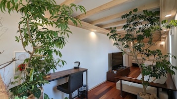 Uma sala de estar moderna com vigas de madeira, uma TV, uma mesa de centro e vários vasos com plantas.