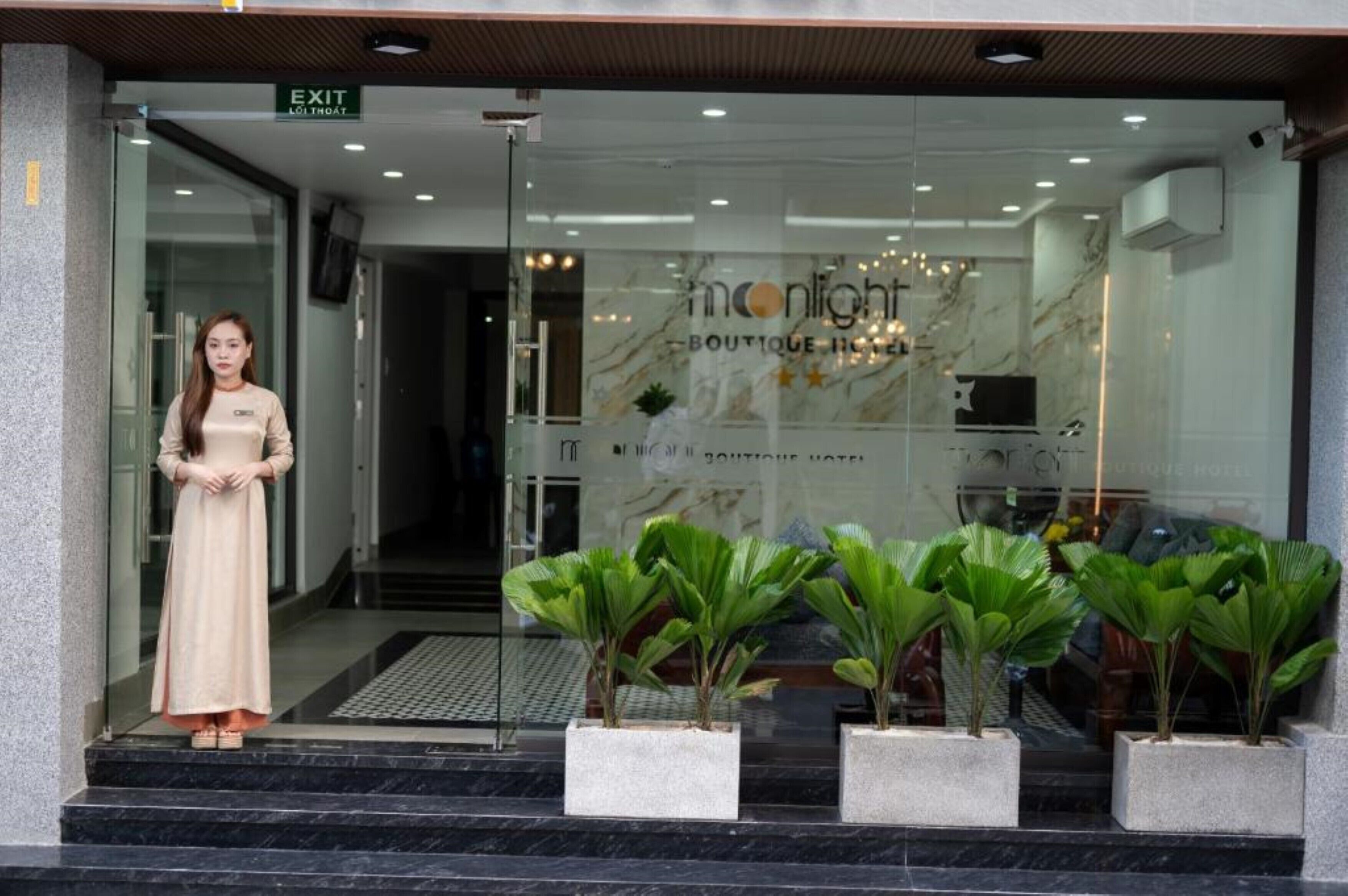 Entrada de um hotel com uma placa que diz "Moonlight Boutique Hotel" e uma mulher parada na entrada.