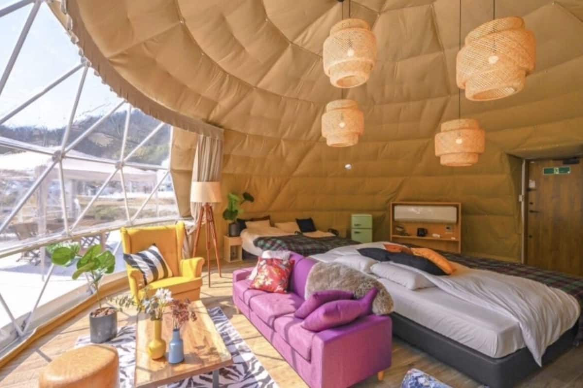 Acolhimento em tenda confortável, com cama, sofá e luminárias pendentes.