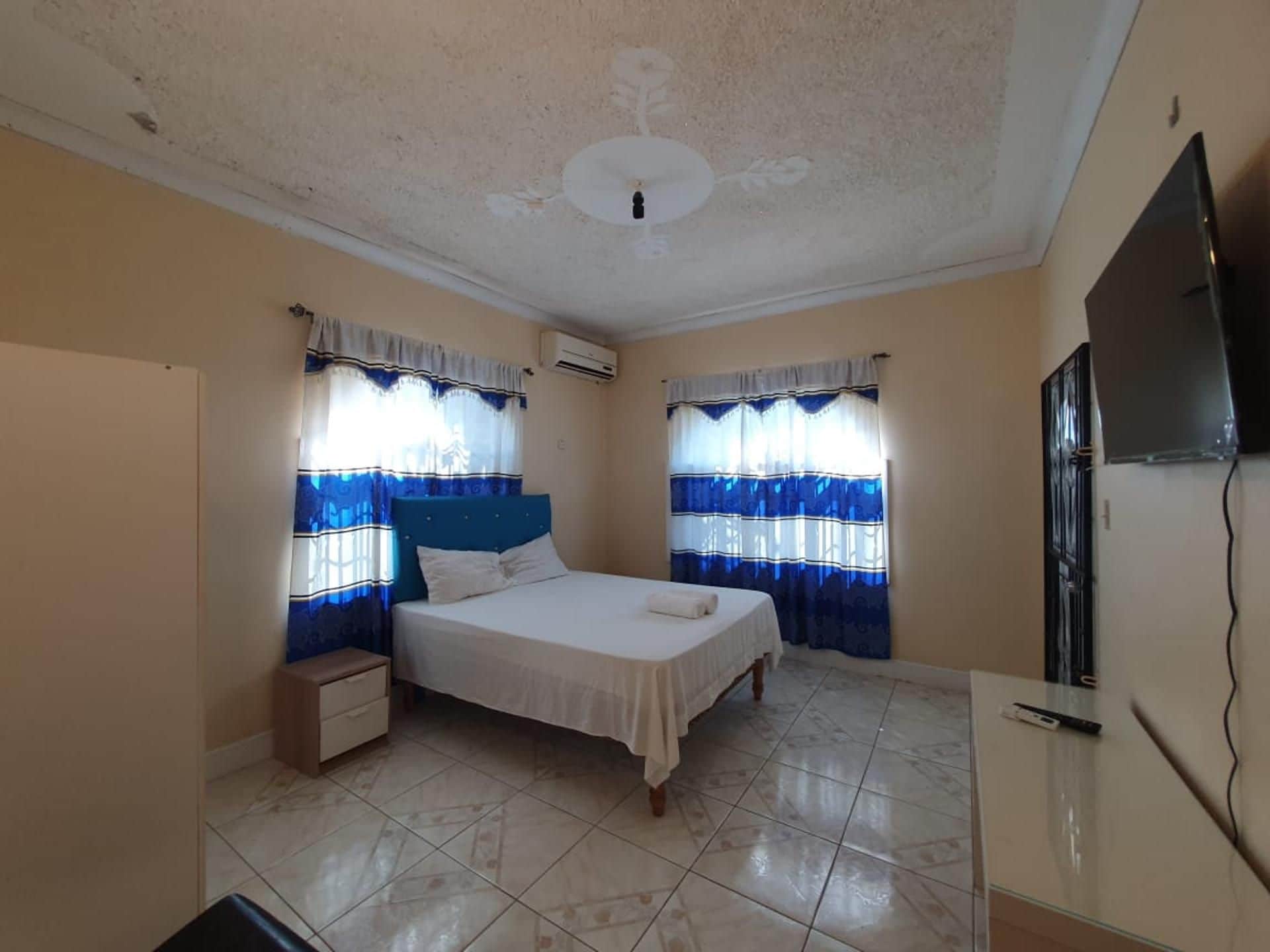 Quarto com cama, mesa de cabeceira e televisão.
