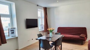 Uma sala de estar moderna com mesa de jantar de madeira, cadeiras pretas, sofá vermelho e TV de tela plana na parede.
