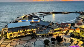 Hotel à beira-mar com um amplo pátio central, uma ponte sobre a água e vista para o mar ao pôr do sol.