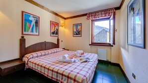 Quarto de hotel com cama, janela com vista para uma casa e obras de arte nas paredes.