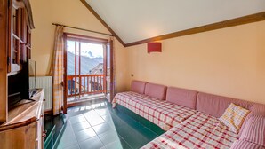 Quarto com sofá xadrez, um armário de madeira e vista para montanhas através de uma porta de varanda.