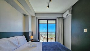 Quarto de hotel com cama, mesa de cabeceira, abajur, ar condicionado e uma janela grande com vista.