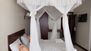 Quarto de hotel com cama sob um dossel, televisão na parede e uma porta ao fundo.