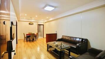 Uma sala de estar com sofá de couro, uma mesa de centro, área de refeições com cadeiras e cozinha com armários.