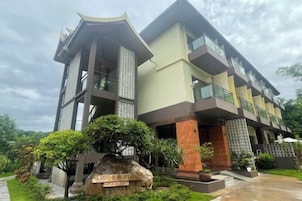 Um hotel moderno com estrutura em vários andares, varandas e um jardim bem cuidado.