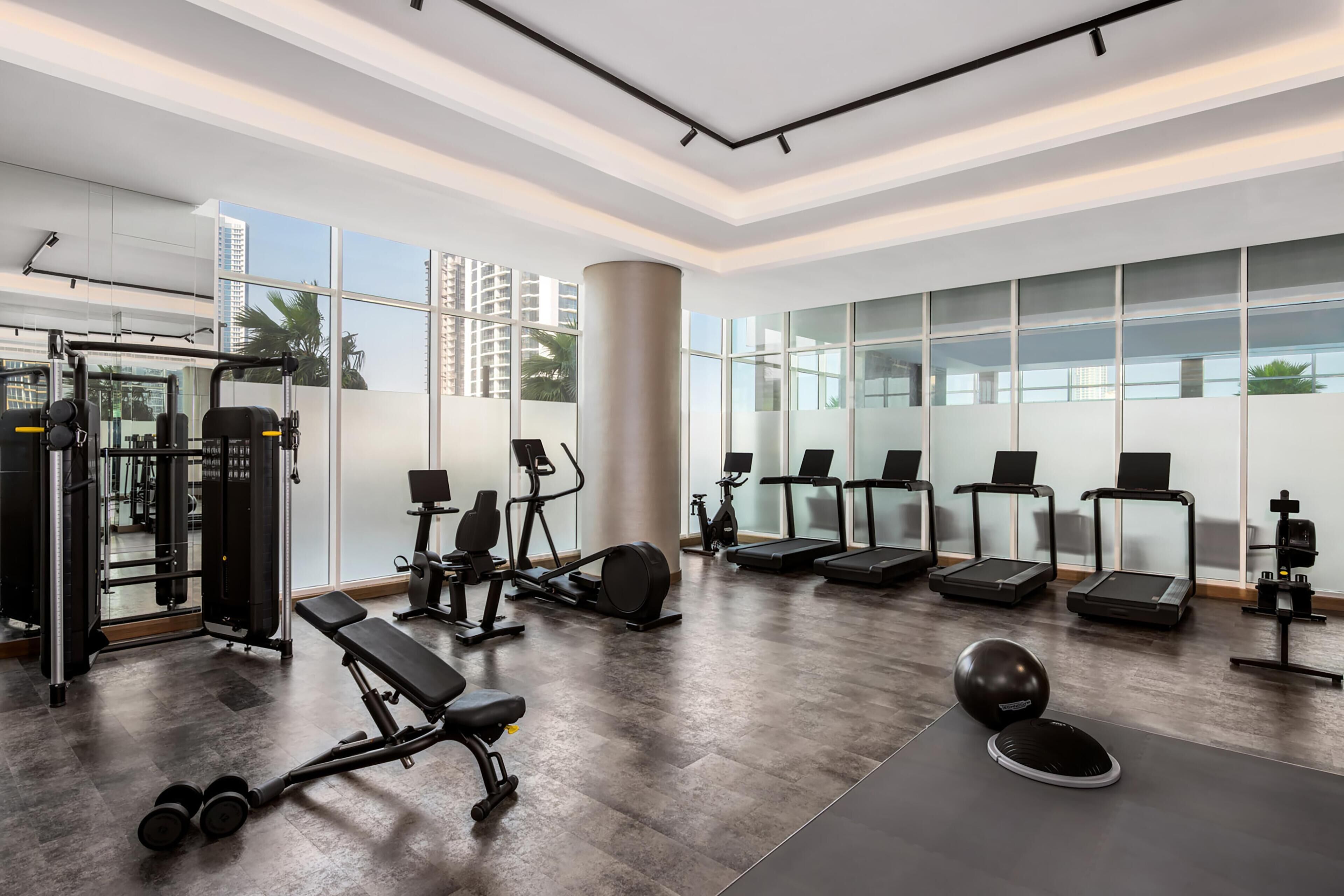 Uma academia moderna com diversos equipamentos de exercício, amplas janelas e um espaço limpo e amplo.