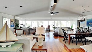 Uma sala de estar ampla com piso de madeira, móveis brancos, um modelo de veleiro e um ventilador de teto.