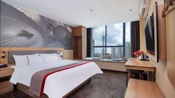 Quarto de hotel moderno com uma cama grande, uma escrivaninha e vista para o horizonte urbano através de grandes janelas.