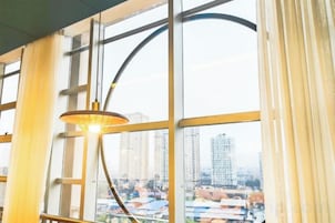 Quarto com janelas amplas, luminária pendente e vista para a paisagem urbana.
