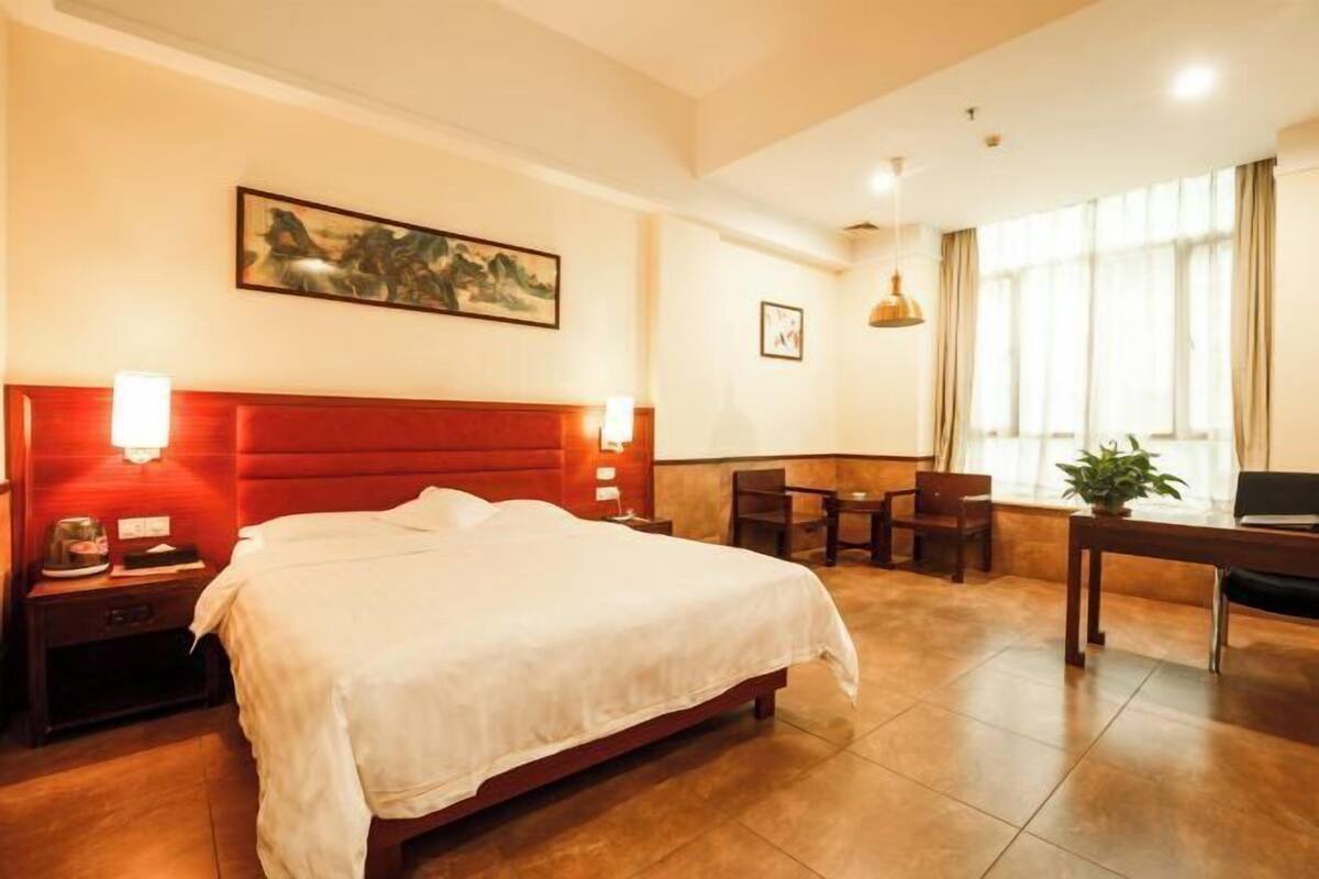 Quarto de hotel com uma cama grande, uma mesa, duas cadeiras, uma mesa de cabeceira e um quadro na parede.