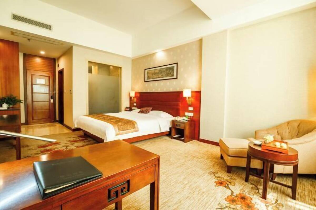 Quarto de hotel com cama, escrivaninha, cadeira e sofá.