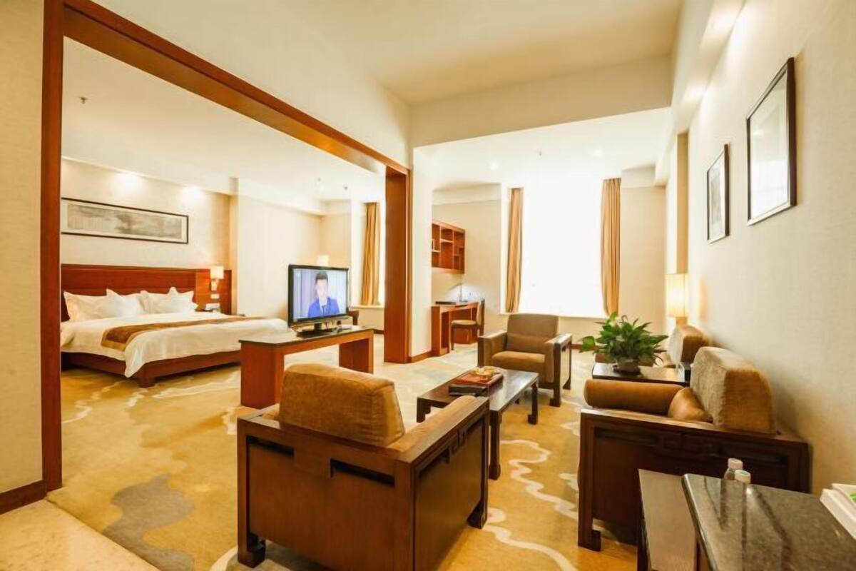 Quarto de hotel com cama, televisão, escrivaninha e área de estar.