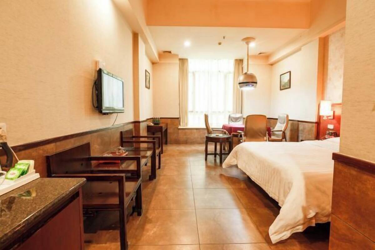 Quarto de hotel com uma cama, uma mesa, uma cadeira, uma televisão e uma janela com cortinas.