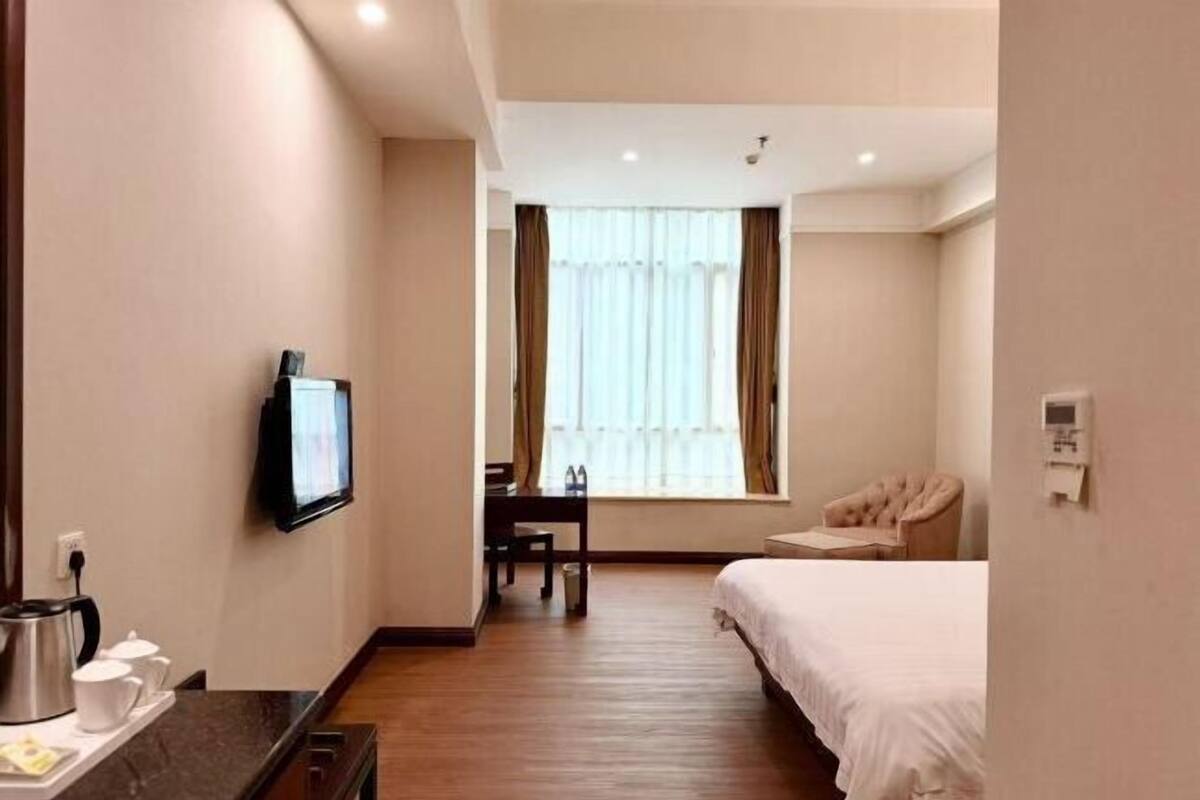 Quarto de hotel com cama, televisão na parede, secretária com cadeira e janela com cortinas.