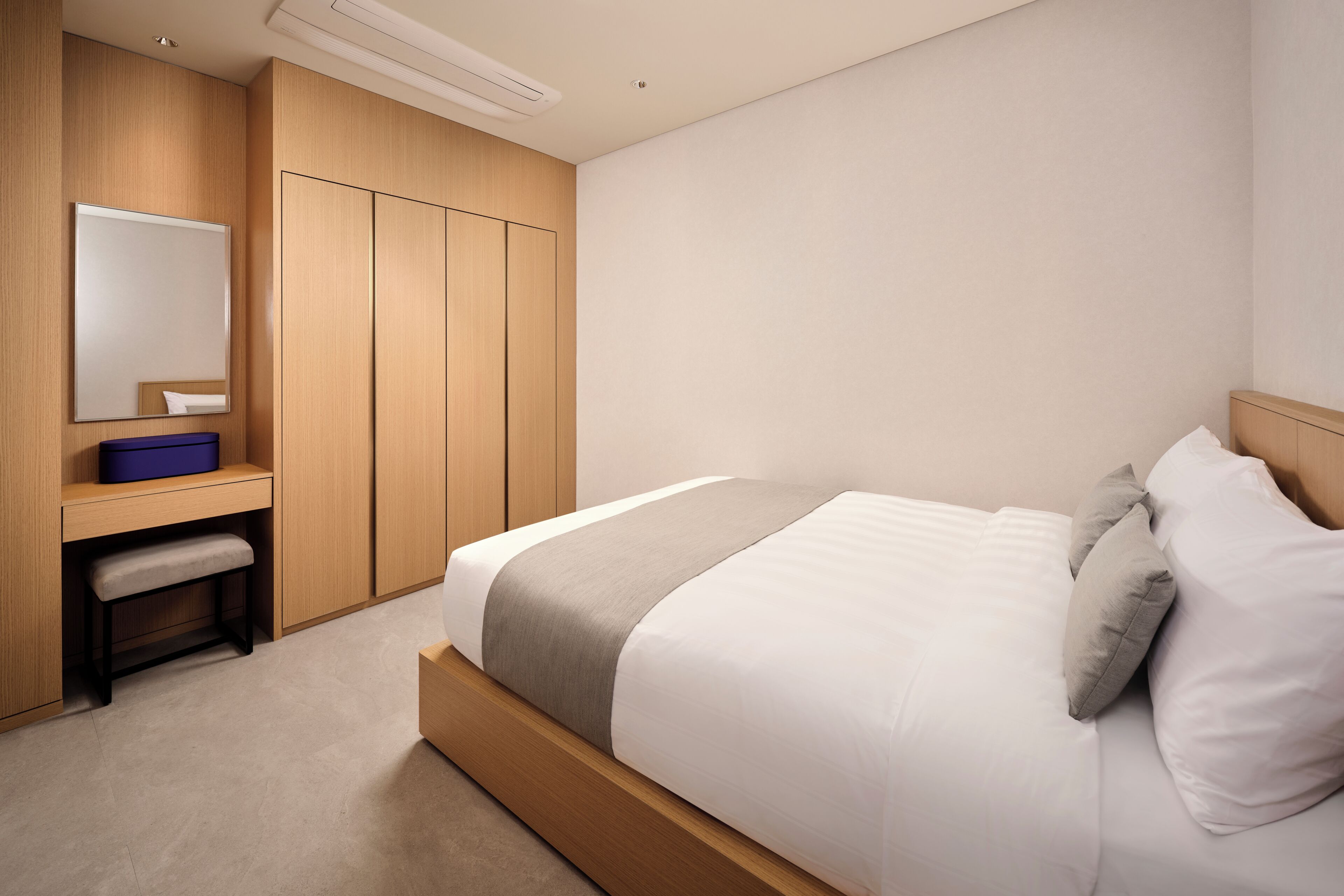 Um quarto com cama, um banquinho, cômoda, espelho e guarda-roupa.
