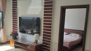 Quarto com cama, televisão, mesa de cabeceira com abajur e espelho.