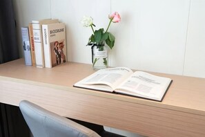 Uma escrivaninha de madeira com um livro aberto, um vaso com flores e livros ao lado.