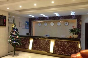 Uma área de recepção de hotel com balcão de mármore, árvore de Natal e relógios na parede.