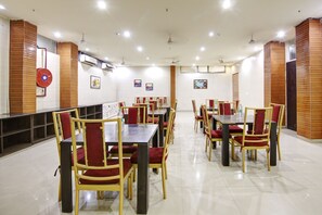 Uma ampla área de jantar com várias mesas e cadeiras, unidades de ar condicionado nas paredes e ventiladores de teto.