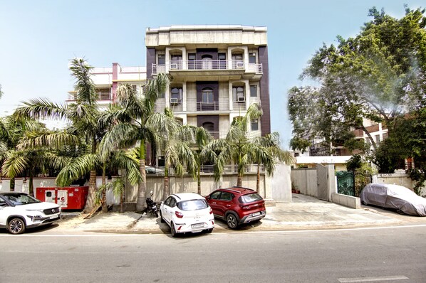 Um edifício residencial com várias andares, varandas, carros estacionados e palmeiras.