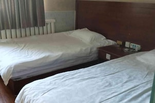 Duas camas de solteiro com cabeceiras de madeira, uma mesa de cabeceira com abajur e uma janela com cortinas.