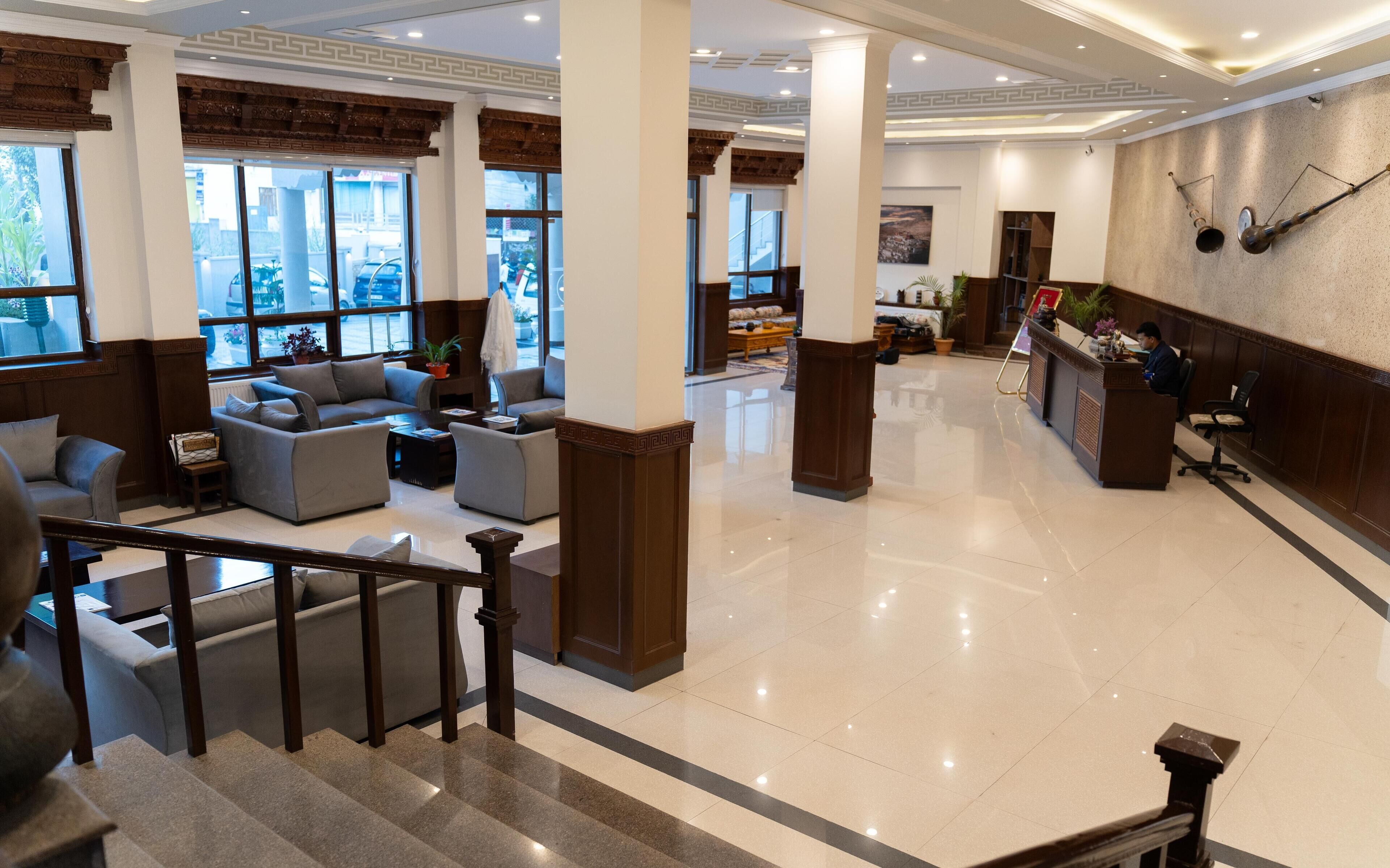 Um hall amplo com área de estar, balcão de recepção e escada para os andares superiores.