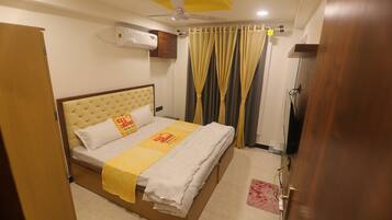 Quarto de hotel com cama, ventoinha no teto, ar condicionado e cortinas.