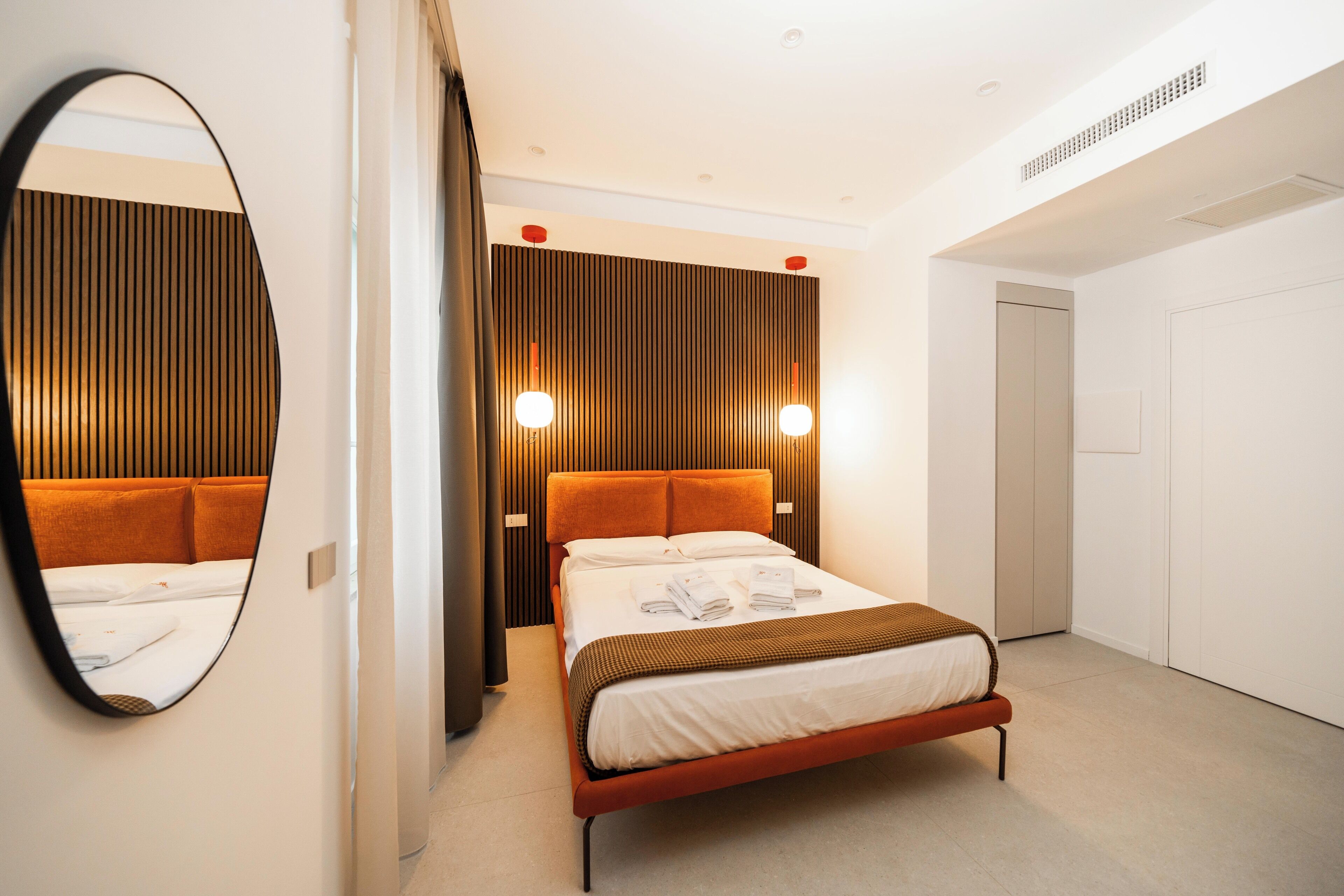Quarto de hotel moderno com uma cama, um espelho, um painel de parede de madeira e um guarda-roupa.