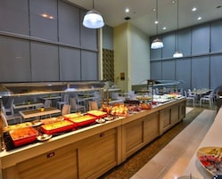 Uma área de buffet com diversos alimentos e disposição de mesas e cadeiras.