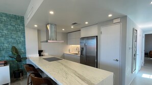 Cozinha moderna com bancada de mármore, eletrodomésticos de aço inoxidável e uma ilha embutida com banquetas.