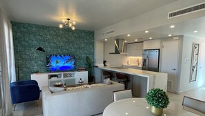 Uma sala de estar moderna com televisão de tela plana, um sofá, uma mesa de jantar e uma cozinha com geladeira e armários.