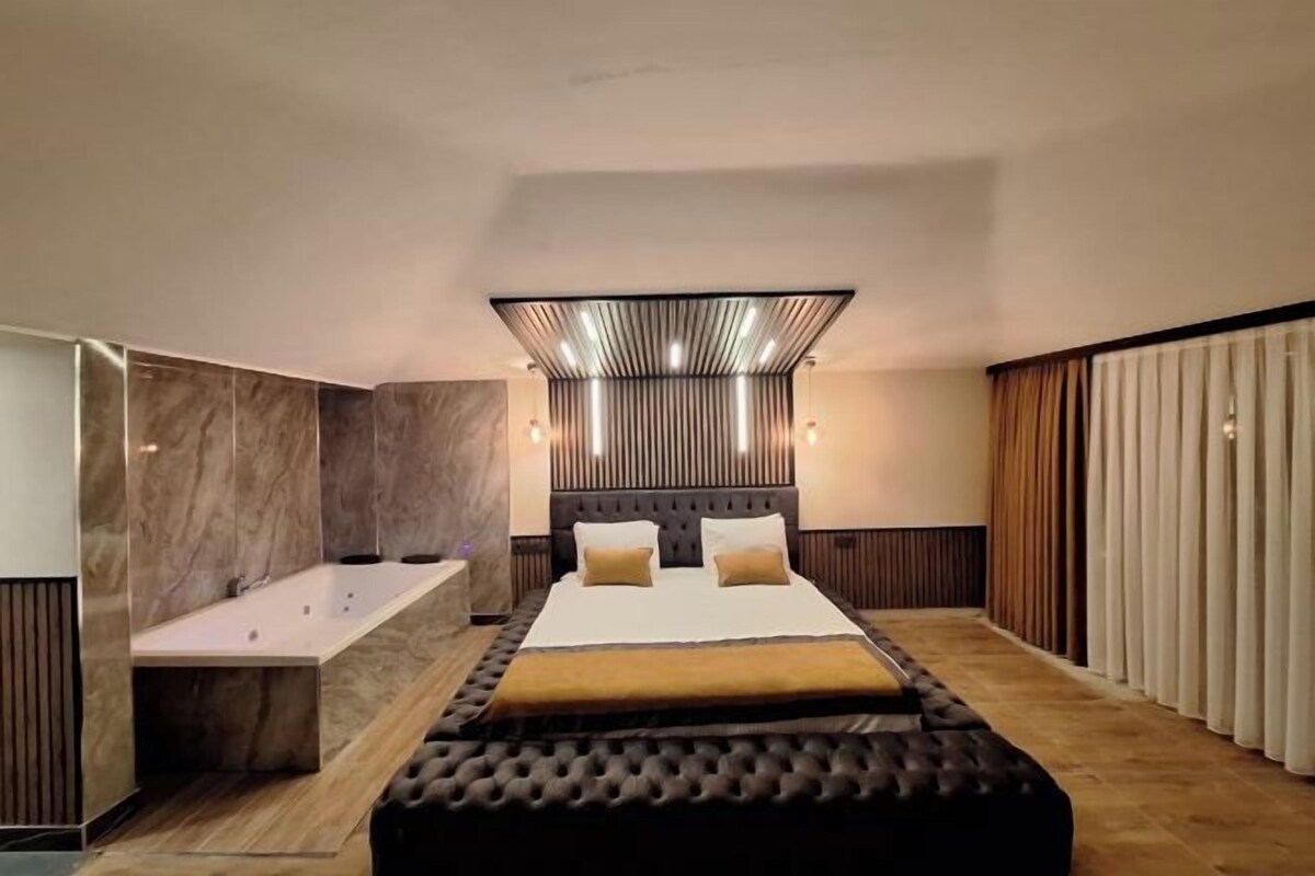 Quarto moderno com cama grande, banheira integrada e piso de madeira.