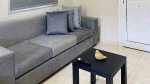 Uma sala de estar com um sofá cinzento, uma mesa de centro preta e uma porta branca.