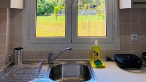 Uma cozinha com uma pia dupla, uma janela com vista para áreas verdes e um ar condicionado instalado no teto.