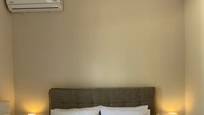 Quarto de hotel com uma cama, duas luminárias de cabeceira, ar condicionado e radiador.