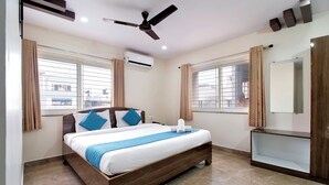 Quarto de hotel moderno com cama grande, ar condicionado, ventoinha no teto e janelas amplas.