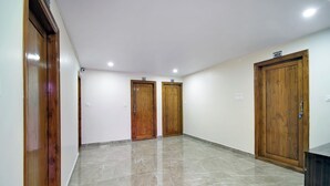 Um corredor com portas de madeira, piso de mármore e teto com iluminação embutida.