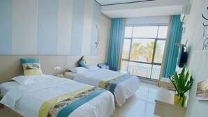 Quarto de hotel com duas camas, uma pequena escrivaninha, janela com cortinas e uma planta.